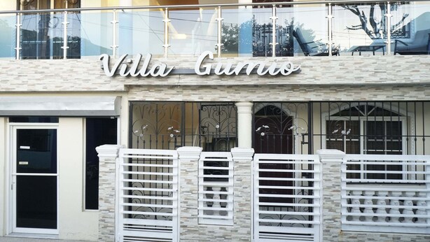 Villa Gumio com fachada de pedra, uma varanda com guarda-corpo de vidro e uma placa sobre a entrada.