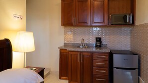 Uma cozinha de hotel compacta com armários de madeira, micro-ondas, pia e geladeira.