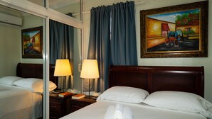 Quarto de hotel com cama, duas luminárias de cabeceira, mesa de cabeceira, quadro e janela com cortinas.