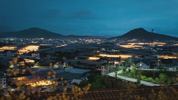 Vista noturna de uma cidade com edifícios iluminados e uma colina imponente ao fundo.
