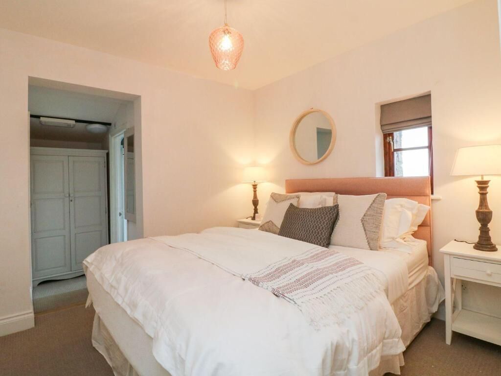 Quarto com cama, luminárias de cabeceira, espelho e guarda-roupa.