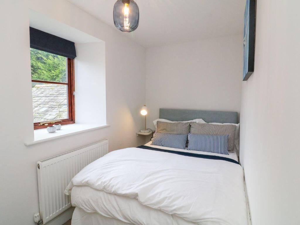 Quarto com cama, mesa de cabeceira, abajur, janela com vista e radiador.