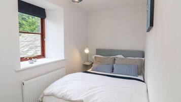 Quarto com cama, mesa de cabeceira, abajur, janela com vista e radiador.