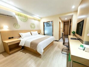 Quarto de hotel moderno com cama, mesa de cabeceira, escrivaninha e televisão.