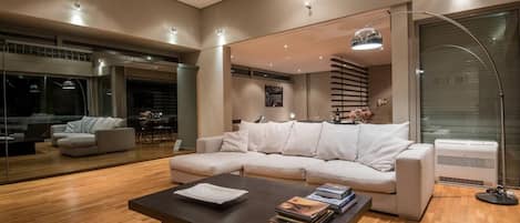 Uma sala de estar moderna com um sofá seccional, uma mesa de centro com livros, um abajur e uma janela grande com persianas.