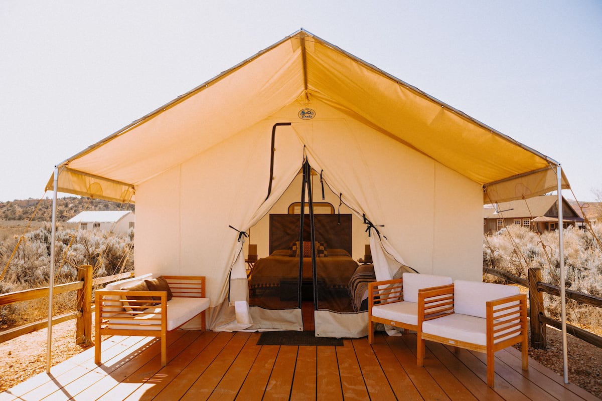 Acomodação em tenda com uma cama, duas cadeiras de madeira e um deck de madeira.