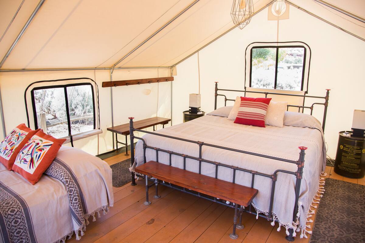 Quarto com tenda, cama, banqueta, mesa de cabeceira e uma janela.