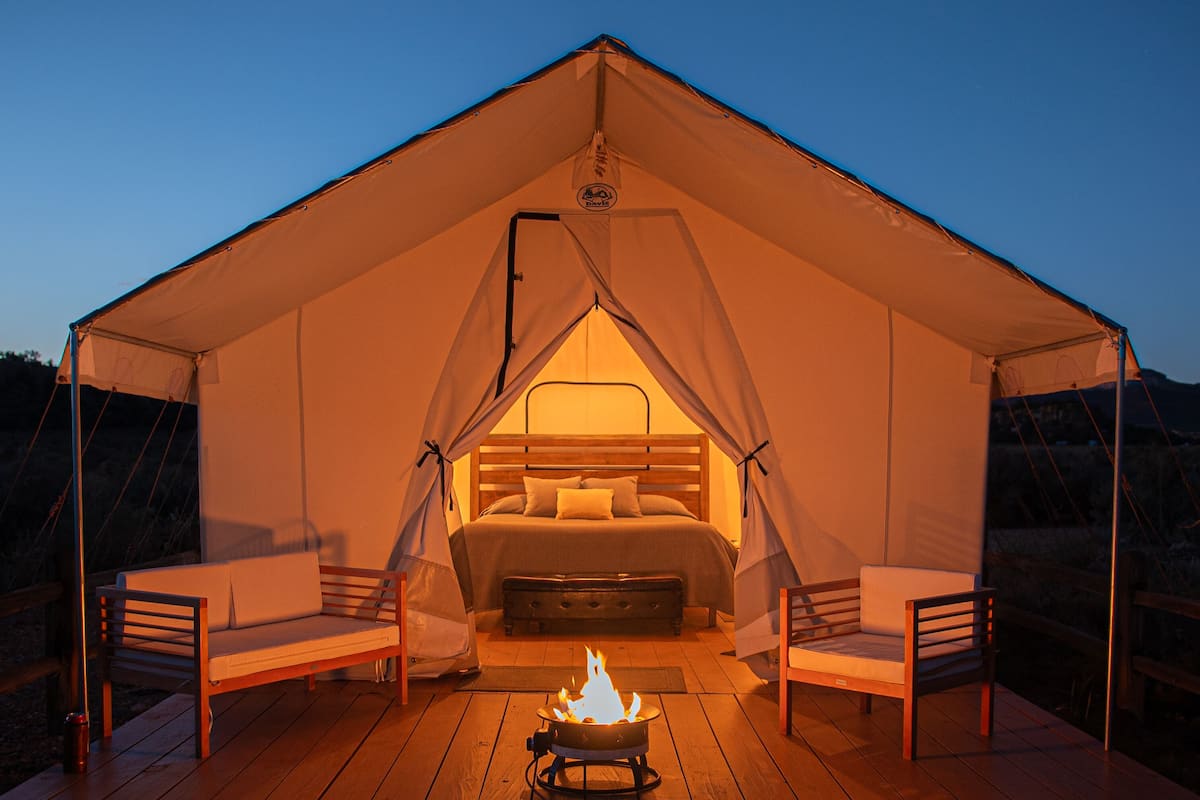 Alojamento em tenda com cama, duas cadeiras e lareira.