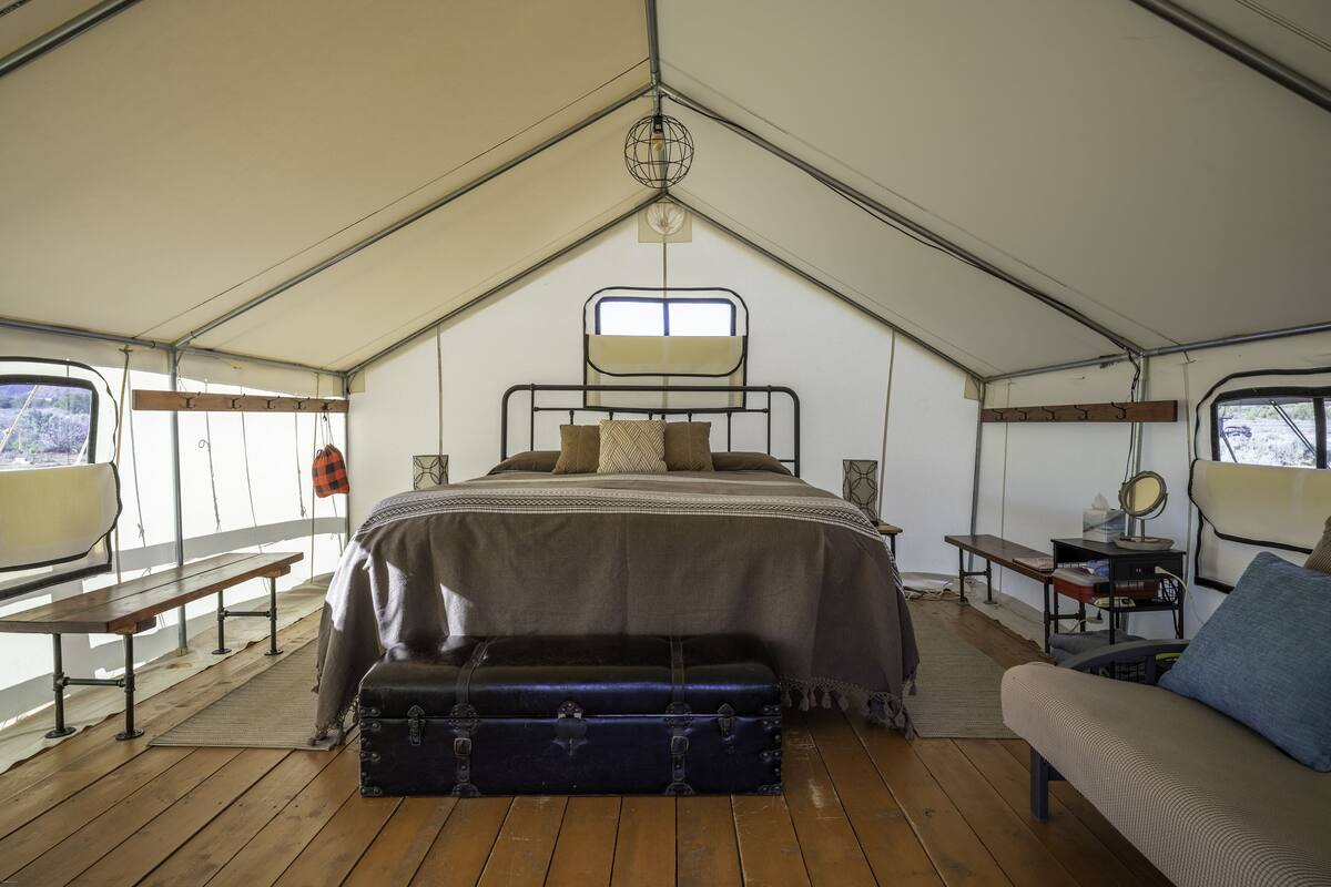 Acomodação em tenda com cama, banco, mala e uma pequena mesa com espelho.