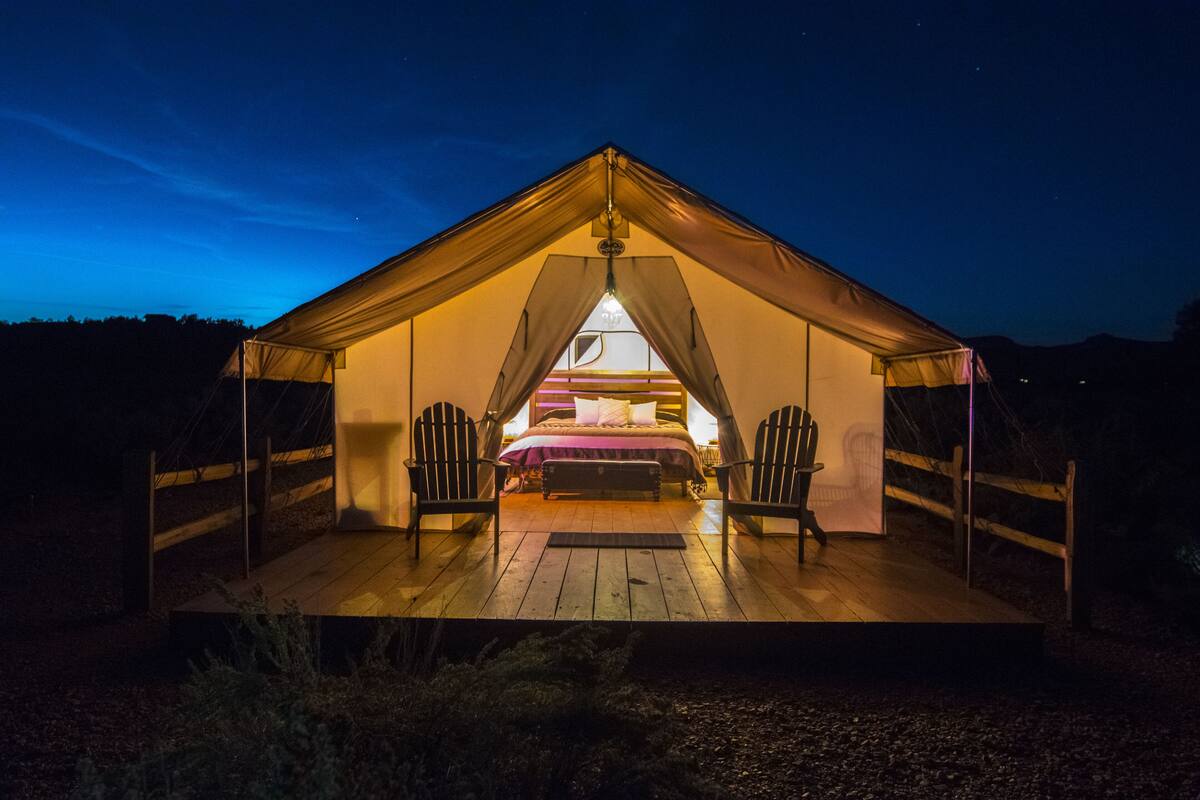 Acomodação em tenda com uma cama, duas cadeiras e um deck de madeira.