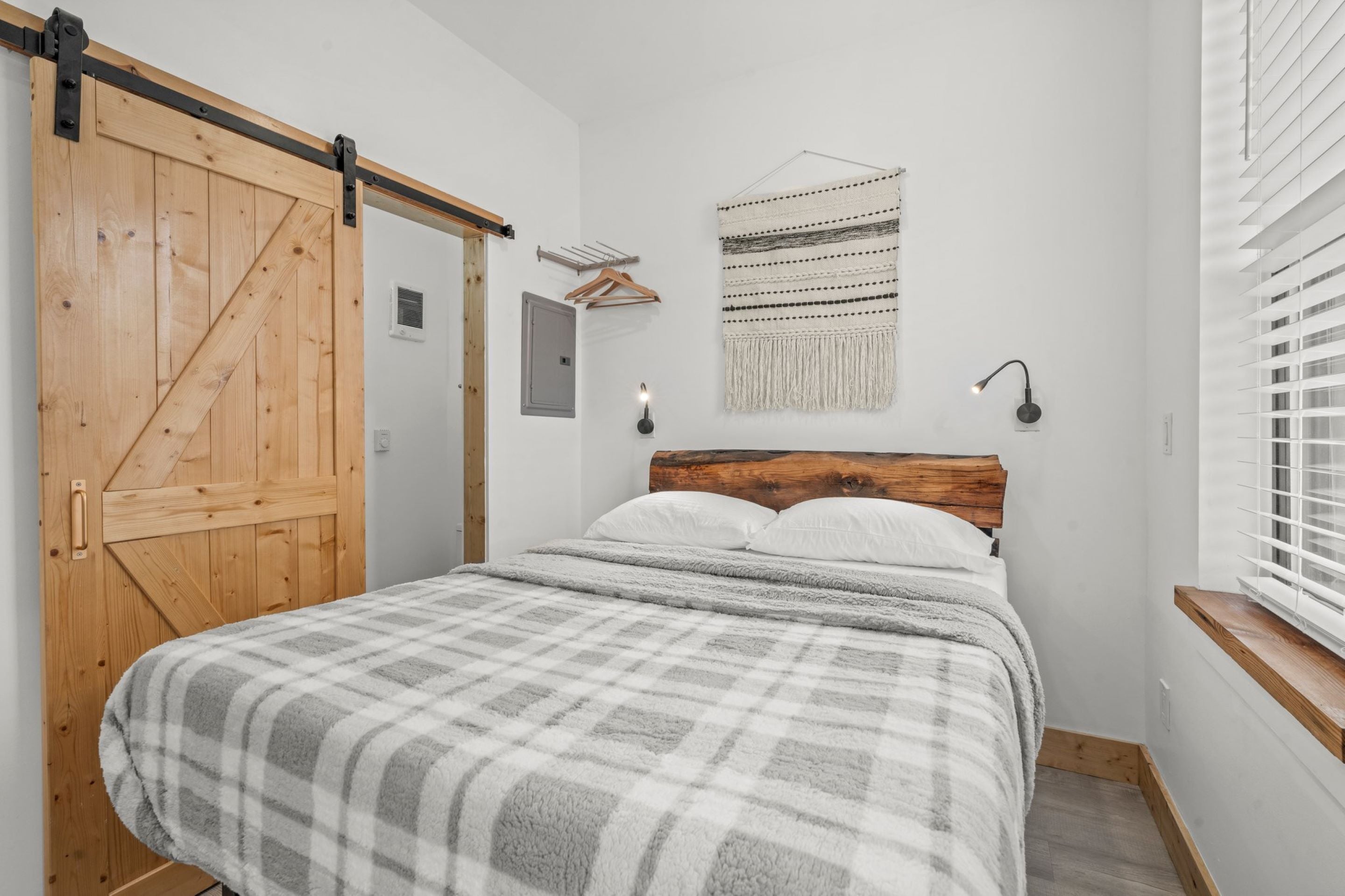 Quarto com cama de madeira, manta xadrez, tapeçaria de macramé e porta de celeiro deslizante.