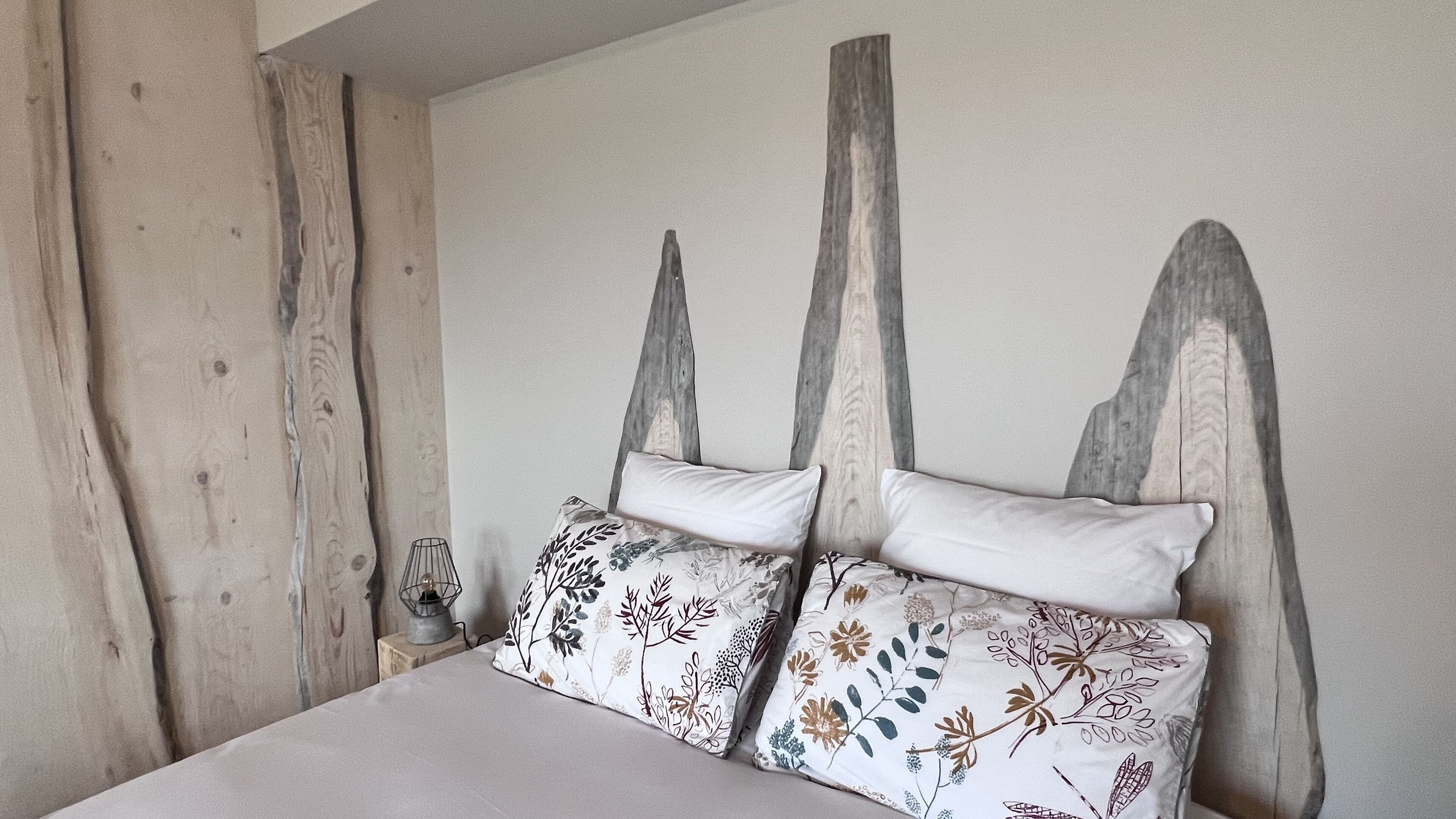 Uma cama com almofadas estampadas em flor e cabeceira lisa.