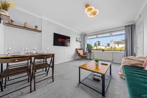 Uma sala de estar moderna com área de jantar, um sofá verde, uma mesa de centro e uma TV exibindo "NETFLIX".