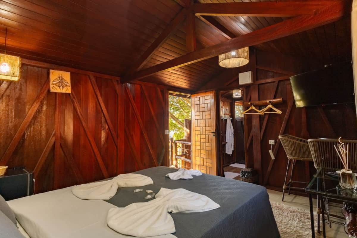 Quarto de madeira com uma cama, uma mesa e um lustre.