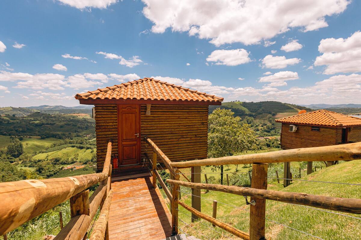 Uma cabana de madeira com uma porta vermelha, uma escadaria de madeira que leva até ela e vista para a paisagem ao redor.