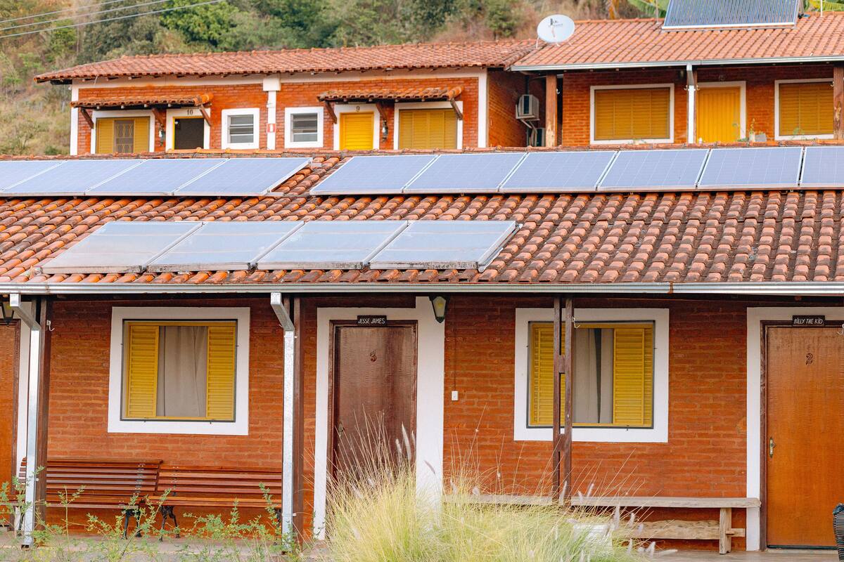 Um edifício com telhado de telhas vermelhas, painéis solares e um banco de madeira na parte externa.