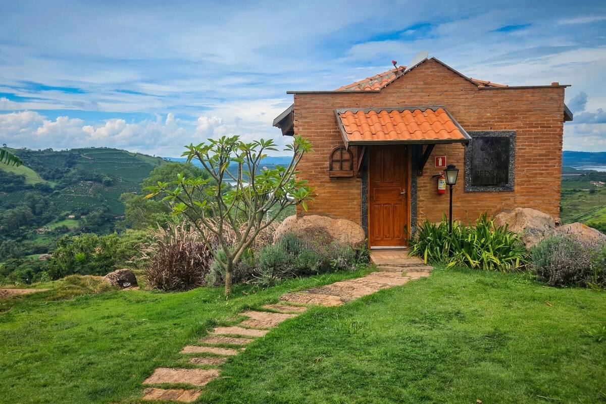 Uma pequena casa de tijolos com telhado em telhas, porta de madeira e um caminho de pedra que a leva.