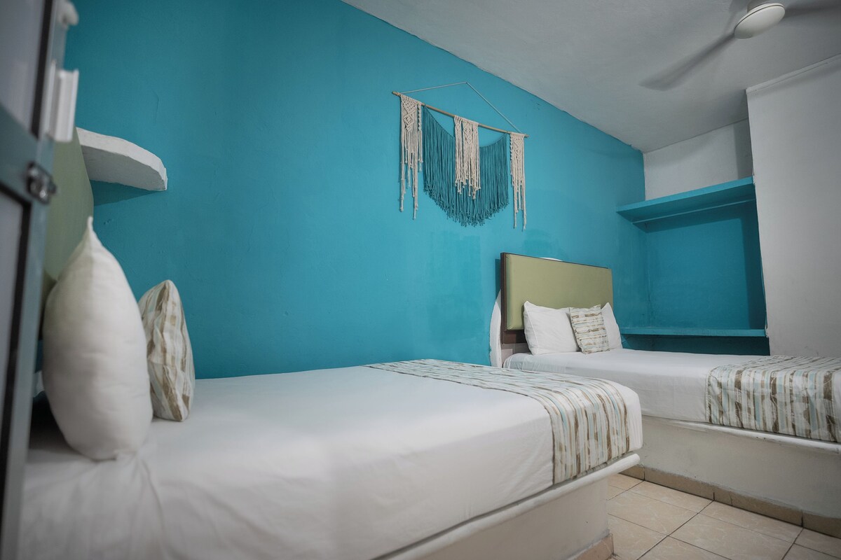 Quarto com duas camas, ventoinha no teto e decoração em macramé fixada na parede.