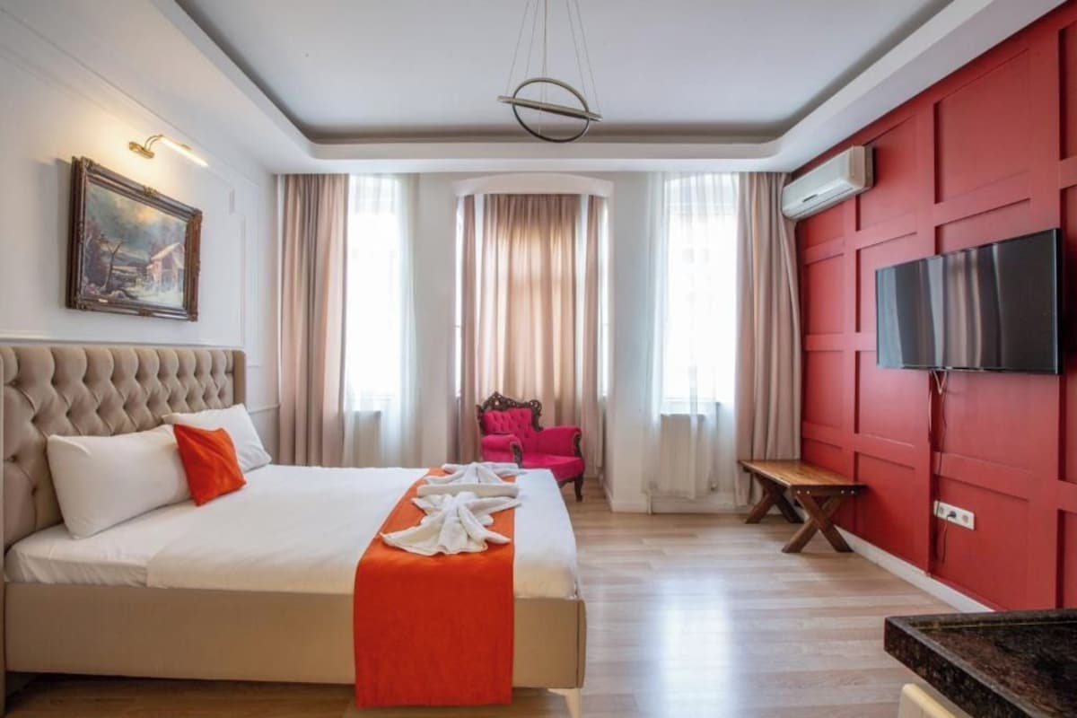 Quarto de hotel com uma cama grande, televisão presa à parede e uma parede com detalhes em vermelho.
