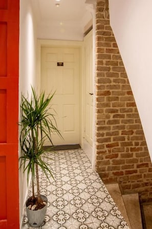 Um corredor com porta branca, planta em vaso e piso estampado.