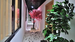 Um corredor estreito com uma árvore rosa decorativa, plantas em vasos e piso de azulejos.