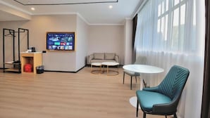 Uma sala de estar moderna com um sofá, duas mesas redondas, uma TV fixada na parede e uma grande janela com cortinas.