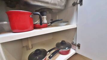 Uma cozinha com bancada branca, uma panela vermelha na prateleira superior e duas panelas vermelhas com tampas na prateleira inferior.