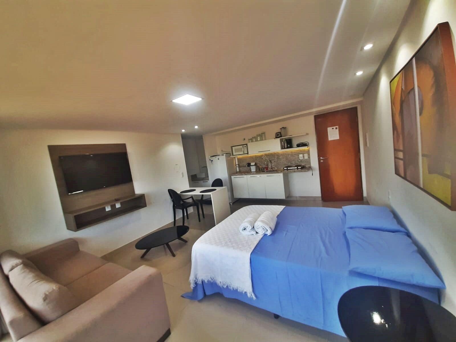 Quarto de hotel com cama, televisão, cozinha compacta e área de estar.