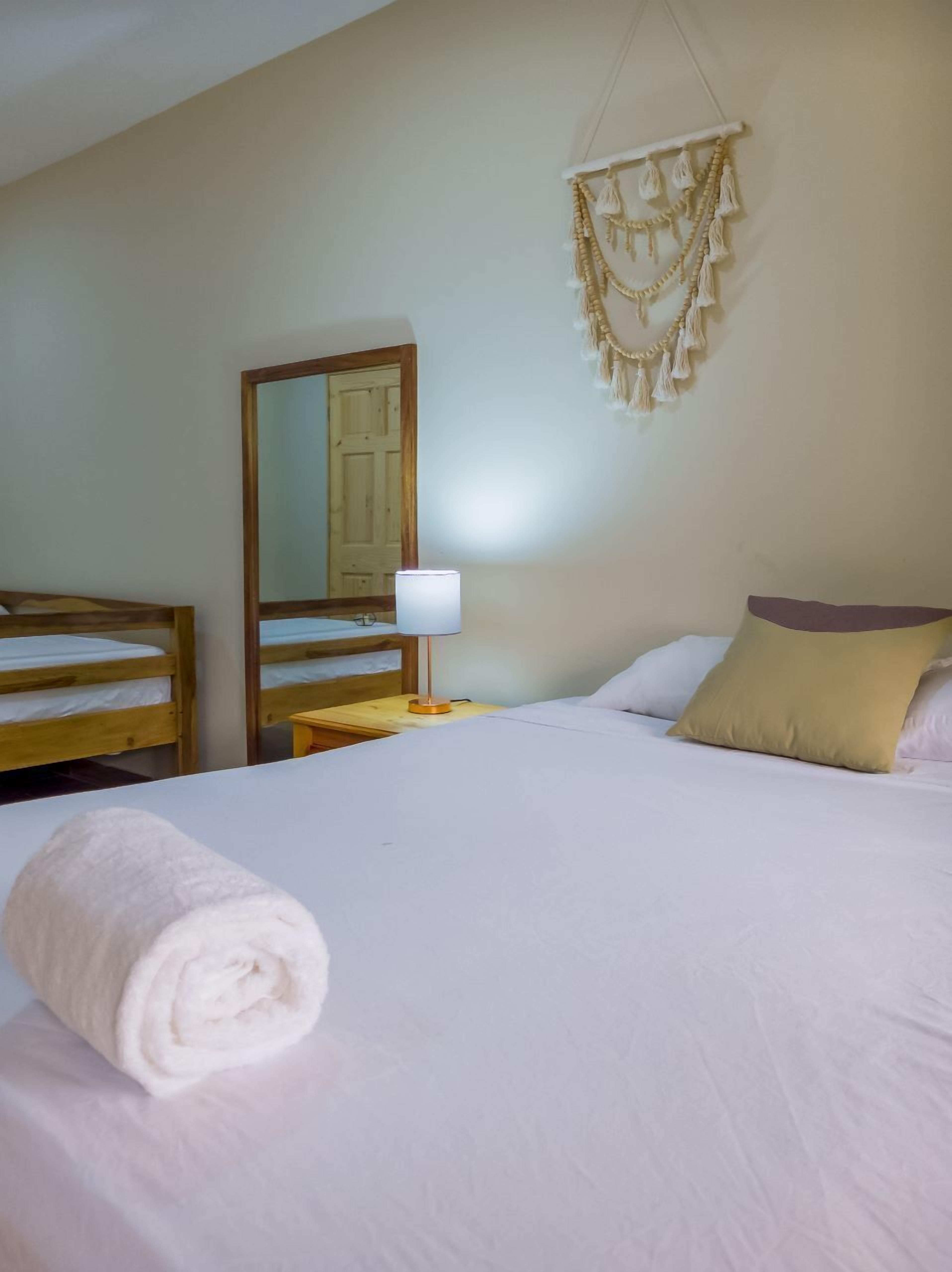 Cama bem arrumada com uma toalha branca enrolada, um abajur e um objeto pendurado na parede.
