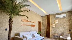 Uma sala de estar moderna com parede de pedra, sofá branco, uma planta grande em vaso e piso de pedra.