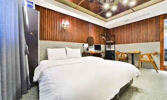 Quarto de hotel com cama, escrivaninha, cadeira, espelho e guarda-roupa.