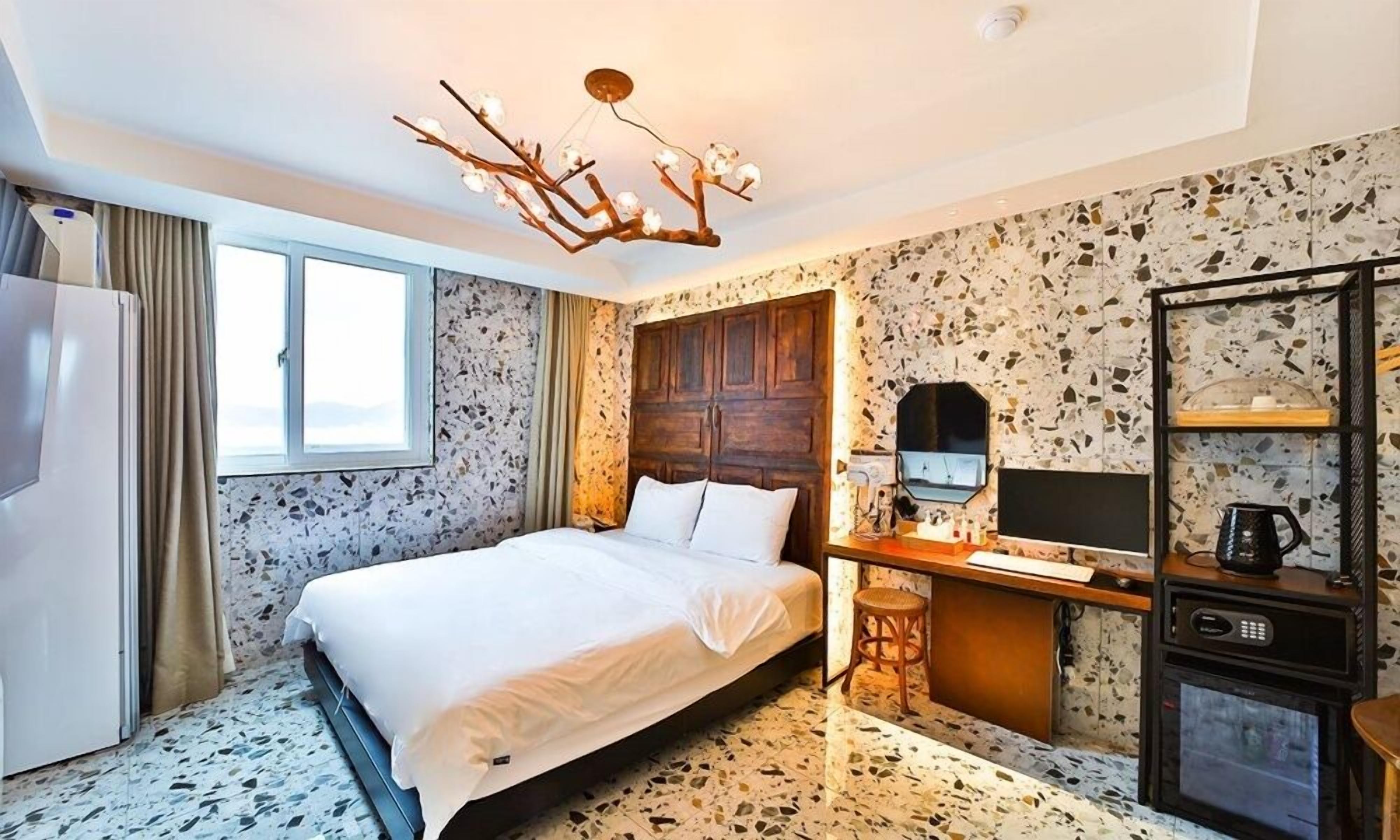 Quarto de hotel com cama, escrivaninha com computador, televisão e minibar.