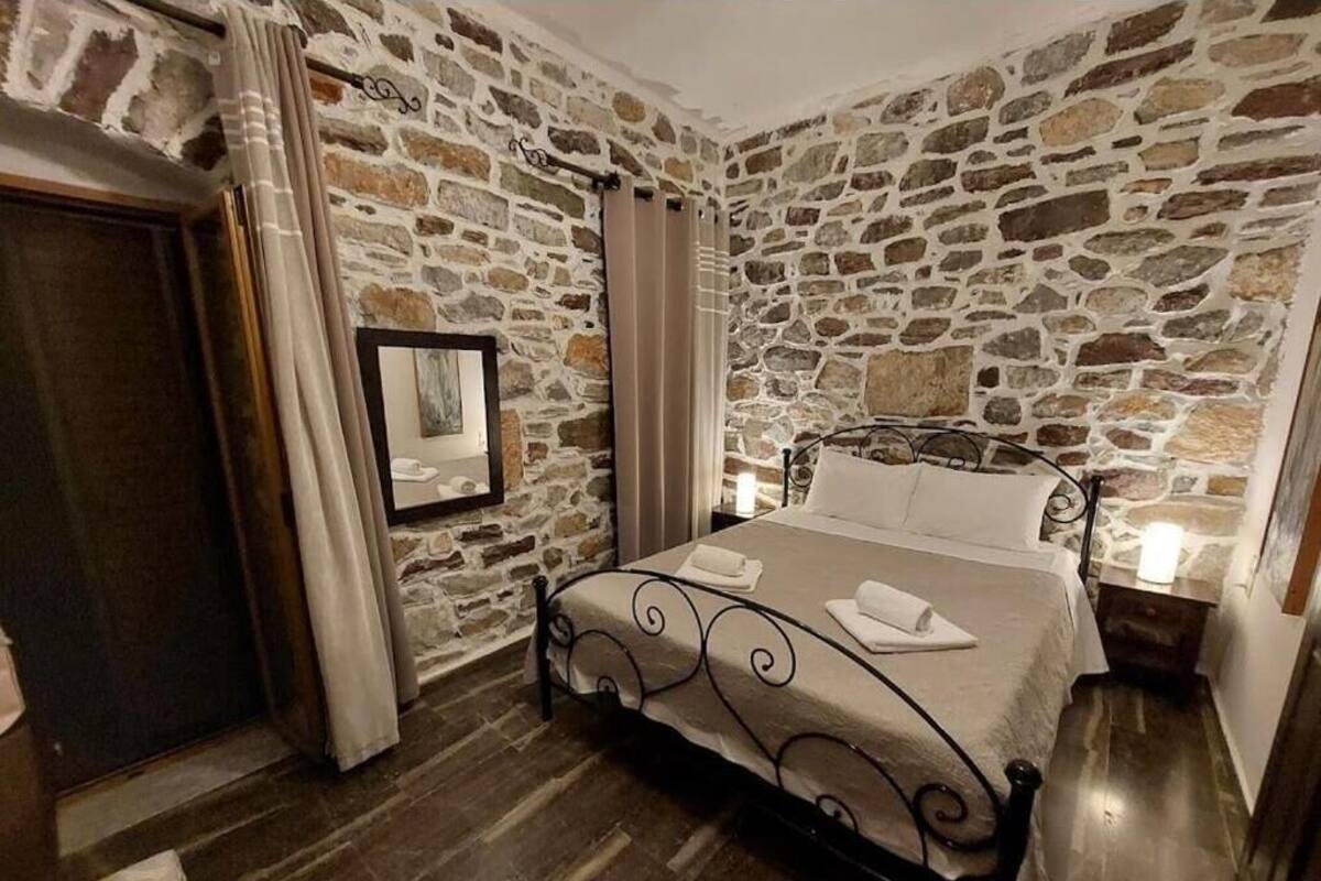Quarto com parede de pedra, cama com estrutura de metal e piso de madeira.