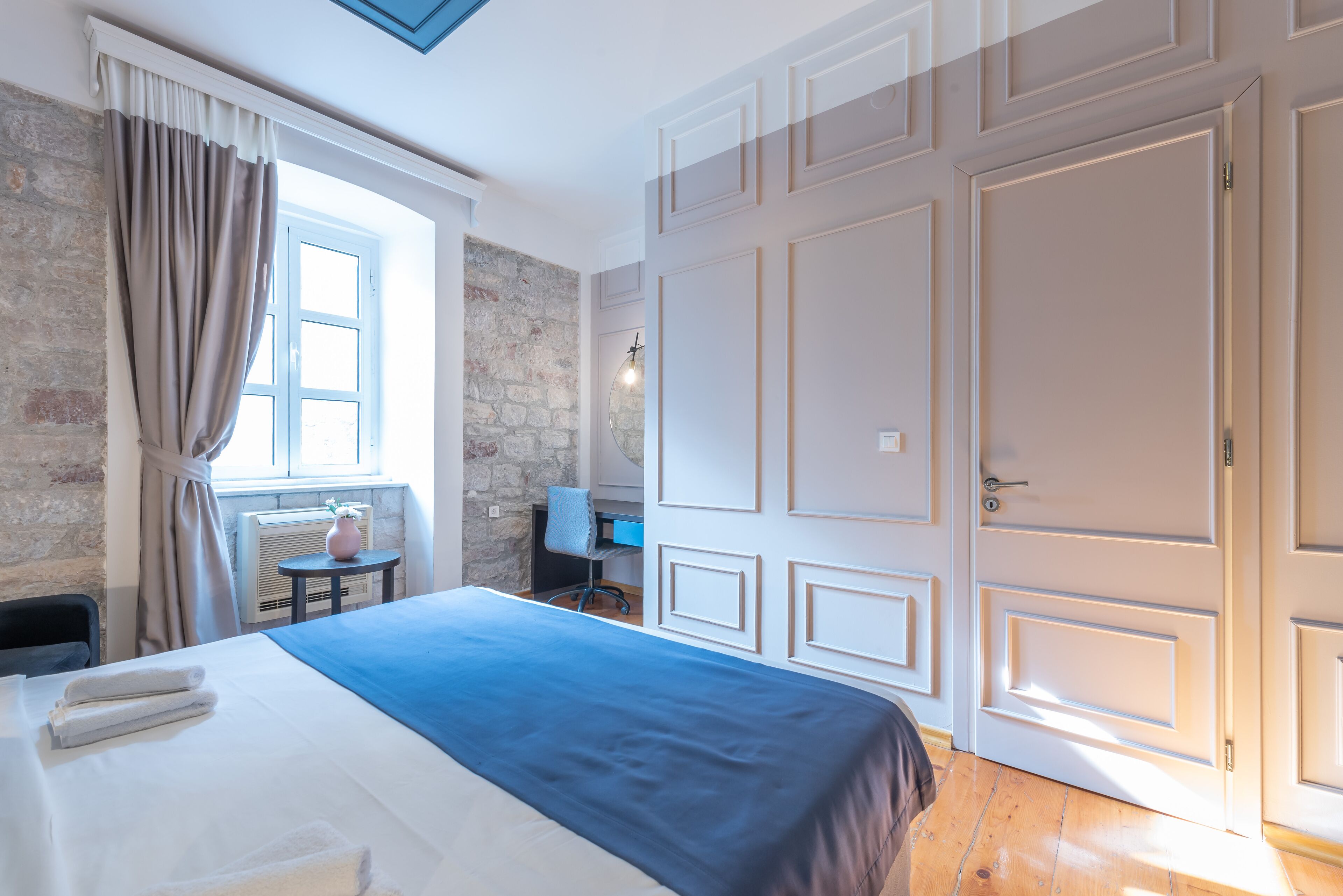 Quarto de hotel com cama grande, escrivaninha, cadeira e guarda-roupa.