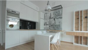 Uma cozinha moderna com armários brancos, uma ilha central com cadeiras e um mural com vista para a cidade na parede.