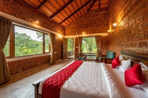 Quarto com cama grande, duas janelas com cortinas, escrivaninha de madeira e vista para área verde.