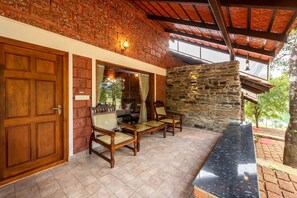 Uma varanda coberta com paredes de pedra, móveis de madeira e uma porta grande.
