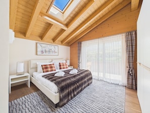 Quarto com claraboia, cama com manta de pele, mesa de cabeceira e janela com cortinas.