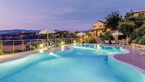 Piscina com espreguiçadeiras e guarda-sóis, em meio a área ajardinada com vista para as colinas.