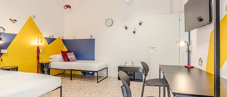 Quarto com cama, escrivaninha, cadeira, televisão e relógio na parede.