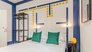 Quarto bem arrumado com cama, almofadas verdes, prateleira na parede com roupas e uma pequena mesa com abajur.