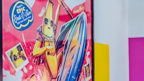 Uma caixa colorida com um personagem de banana segurando uma prancha de surf, cercada por gráficos e texto vibrantes.