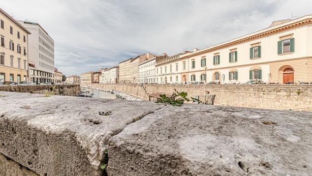 Uma ponte de pedra sobre um canal, ladeada por edifícios históricos com janelas em arco e uma parede de pedra.