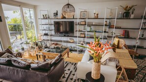 Uma sala de estar moderna com uma televisão grande, assentos confortáveis e uma estante cheia de livros e objetos decorativos.