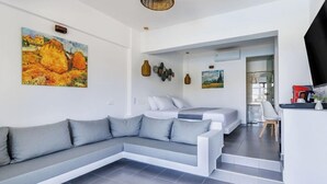 Uma sala de estar moderna com um sofá modular cinza, uma cama branca e um espaço de jantar.