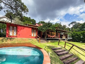 Uma casa vermelha com piscina, rede e deck de madeira.