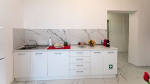 Uma cozinha moderna com armários brancos, painel de backsplash de mármore e uma pia. Há alimentos e uma cafeteira na bancada.