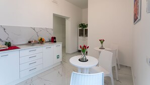 Uma cozinha moderna com armários brancos, painel de parede em mármore e área de jantar com mesa redonda e cadeiras brancas.