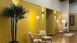 Um hall espaçoso com pé-direito alto, uma grande planta em vaso e áreas de estar com mesas e cadeiras.