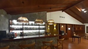 Uma área de bar com cadeiras de madeira, parede de pedra e prateleira com garrafas.
